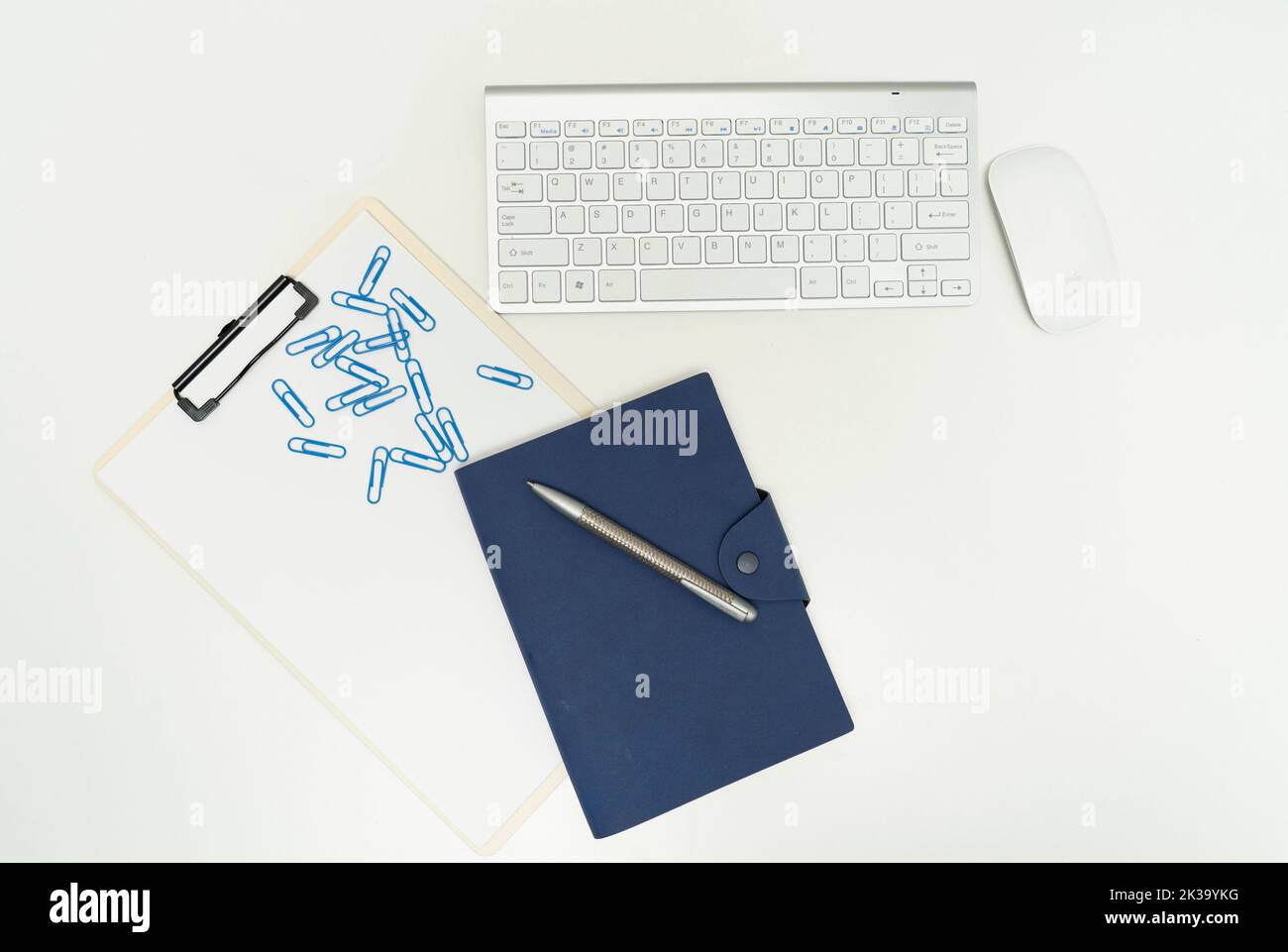 A top view of a mouse and keyboard next to a pen on top of a clipboard ...