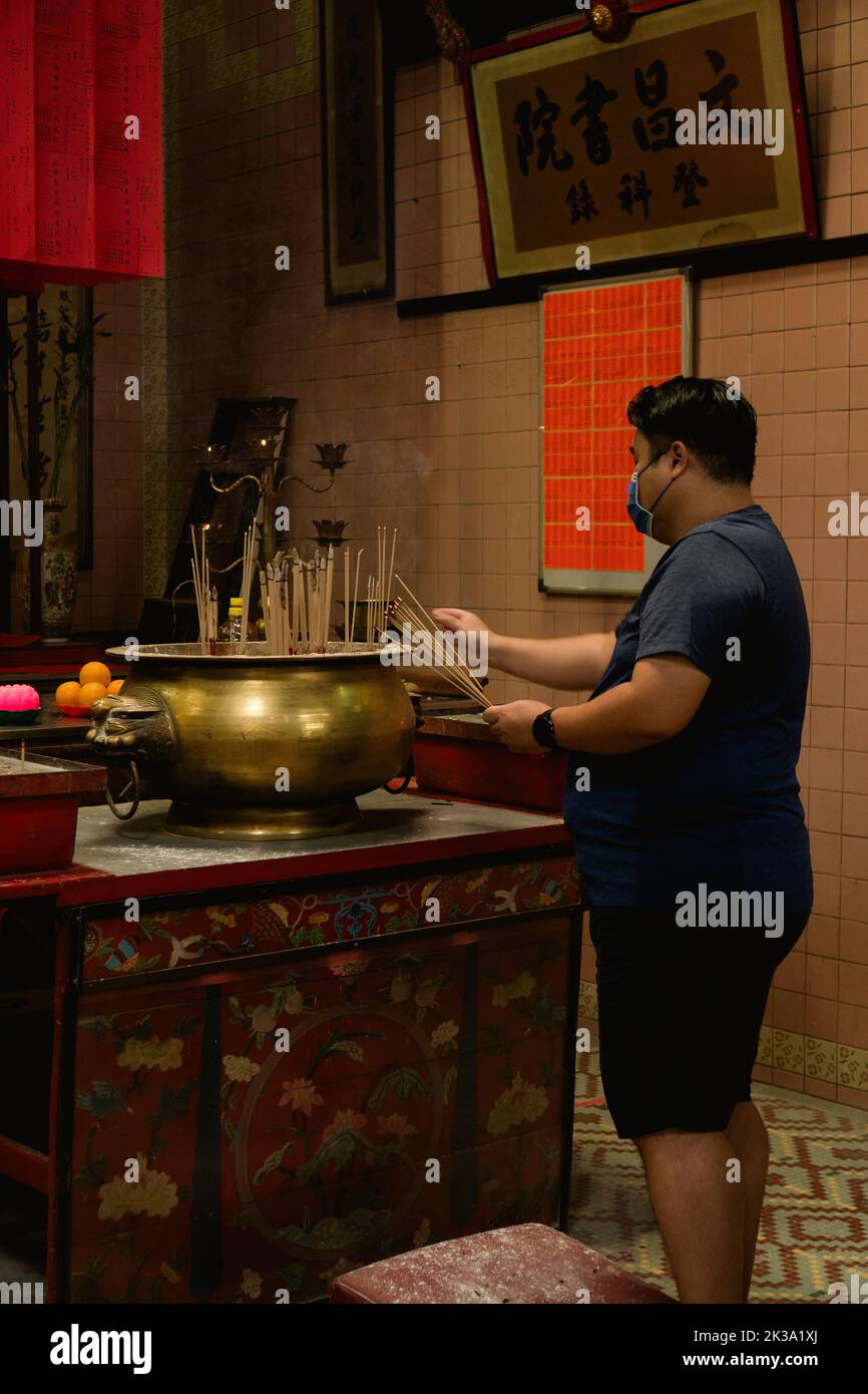 A vertical shot of a Chinese man praying inside the Sin Sze Si Ya ...