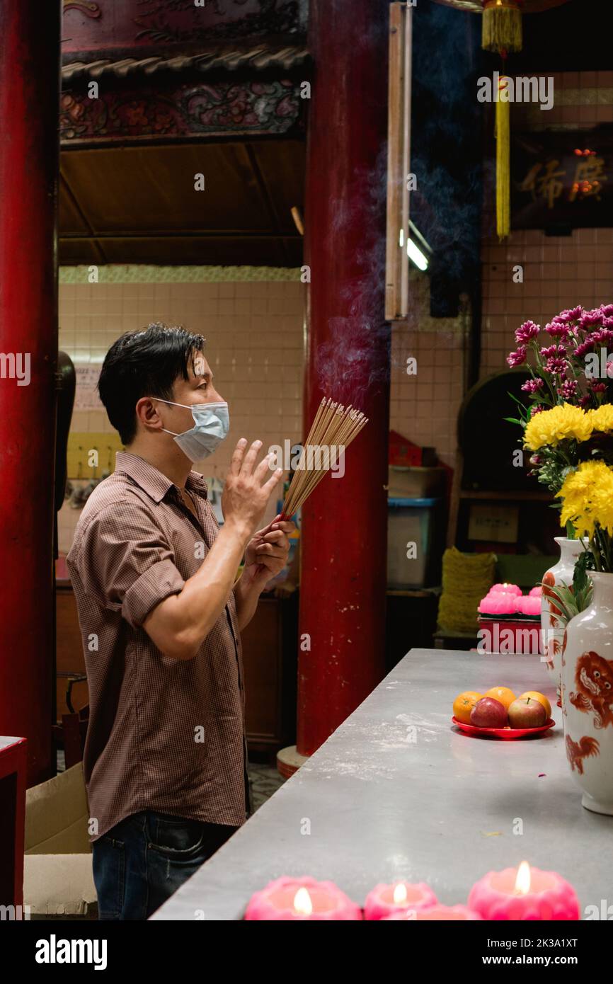 A vertical shot of a Chinese man praying inside the Sin Sze Si Ya ...