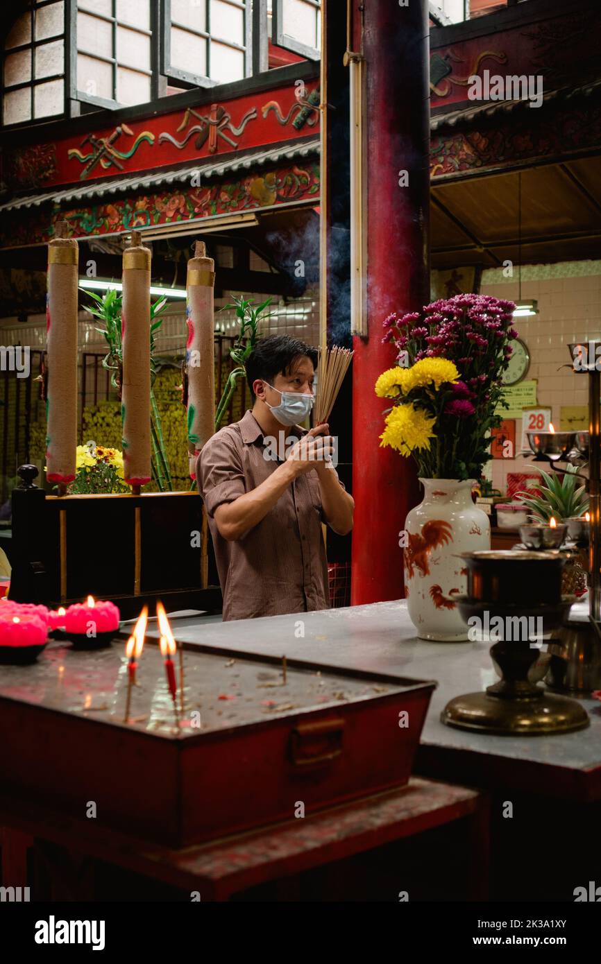 A vertical shot of a Chinese man praying inside the Sin Sze Si Ya ...