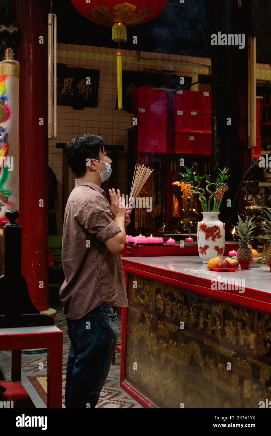 A vertical shot of a Chinese man praying inside the Sin Sze Si Ya ...
