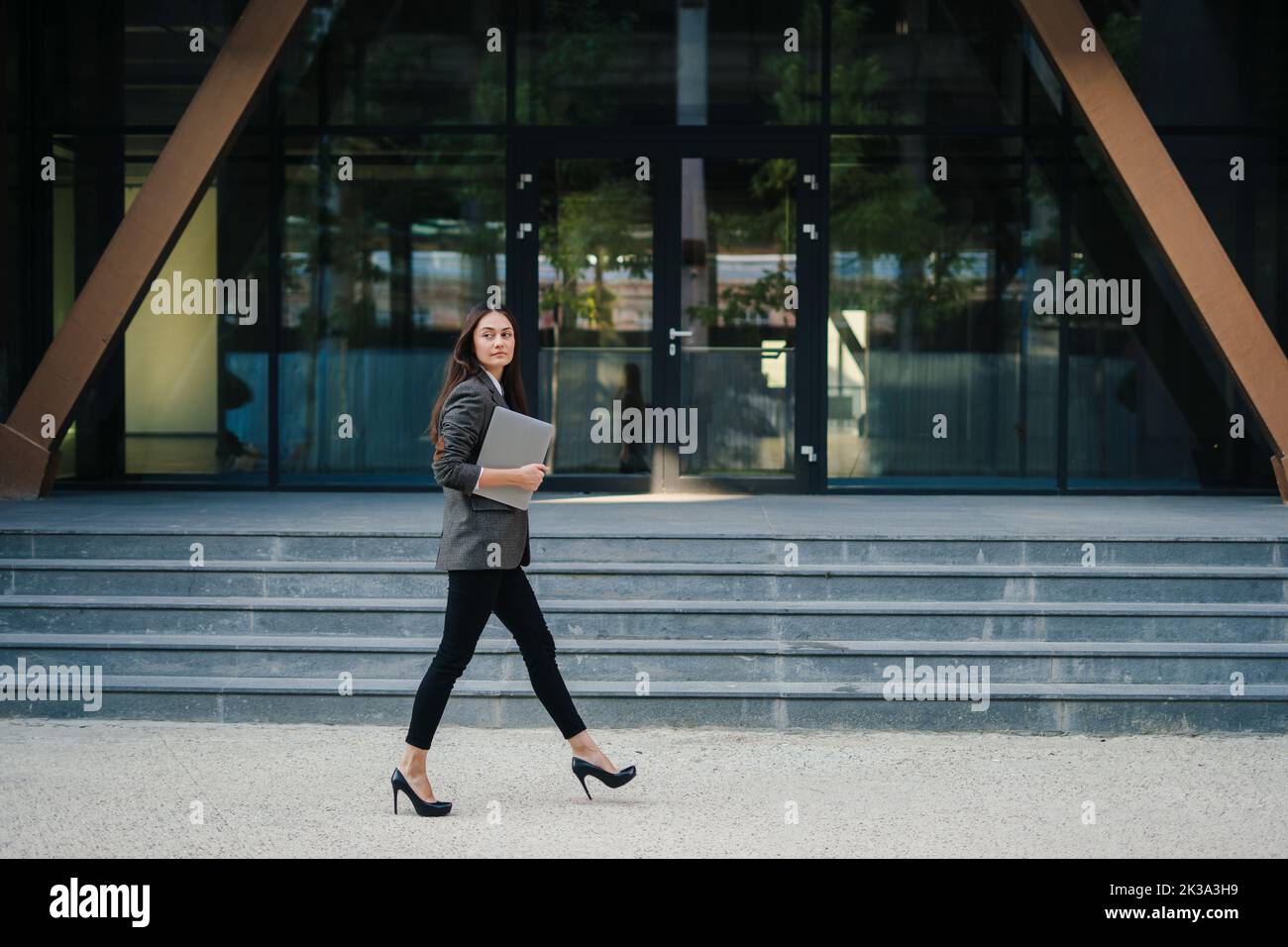 Young businesswoman carrying laptop computer, looking away, walking out ...