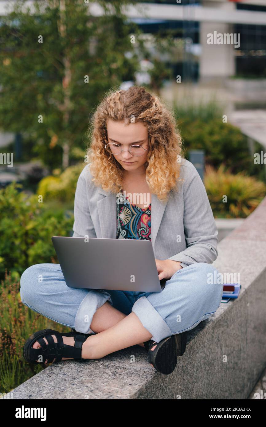 Caucasian curly woman university student sitting outdoors working on ...