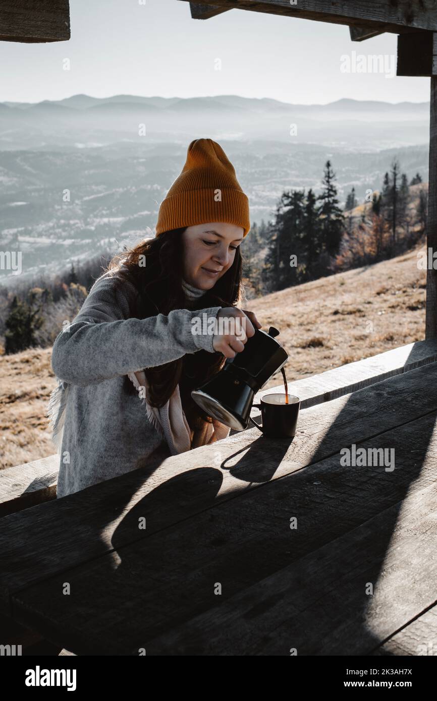 Woman pouring out coffee from Moka pot into a cup outdoors in front of ...