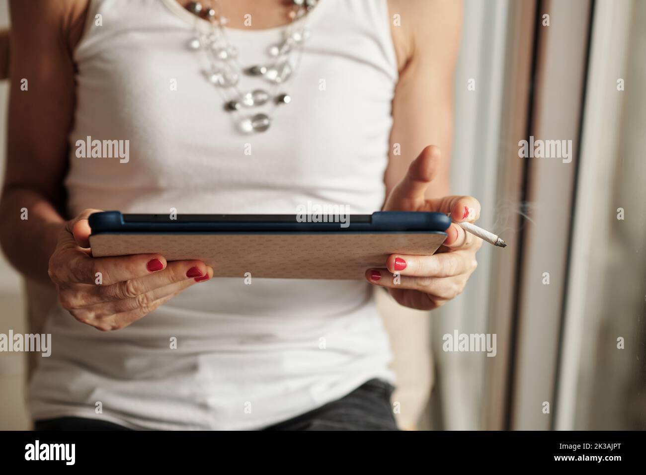 Hands of woman in white tank top smoking cigarette and reading e-book ...