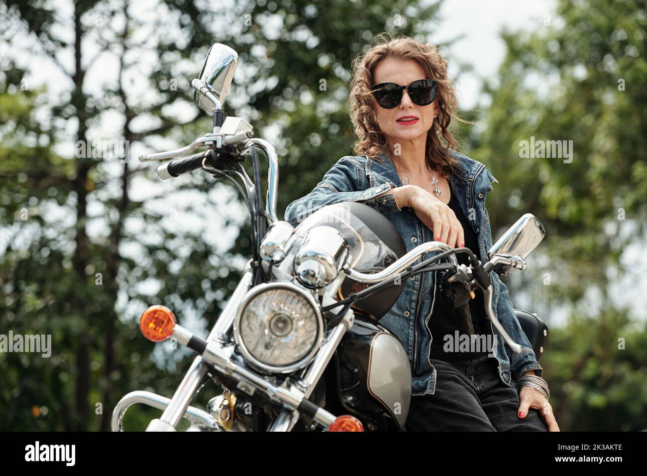 Portrait of glam rock mature woman standing next to her motorcycle and ...