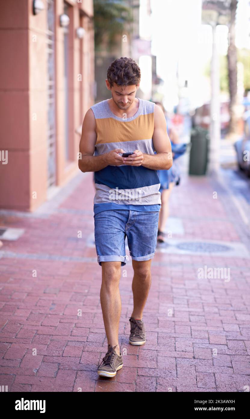Communicating on the move. Full length shot of a young man walking down ...