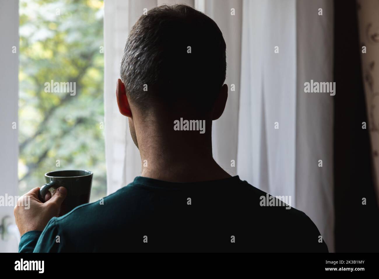 Artistic low key photo with back of young adult man with cup of coffee ...