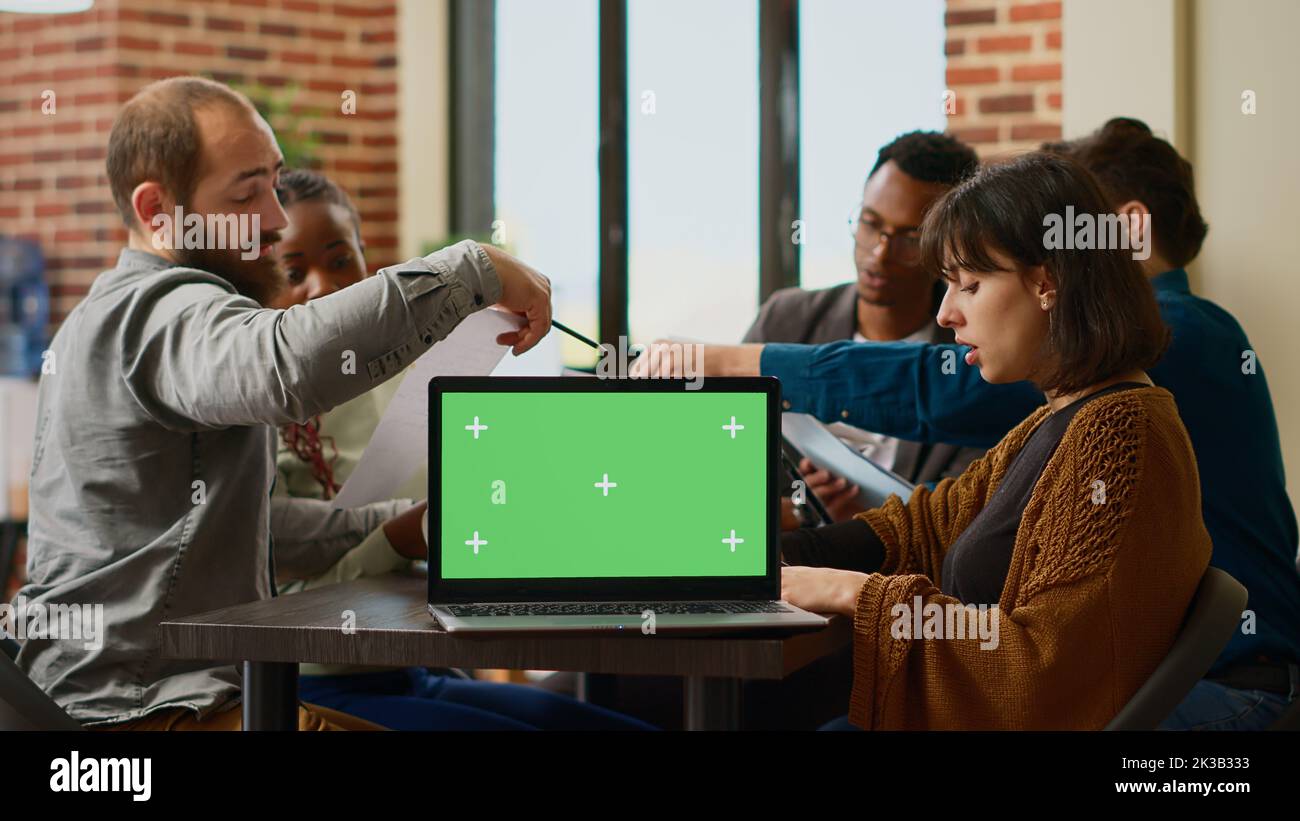 Diverse team of people working with greenscreen on laptop in business ...