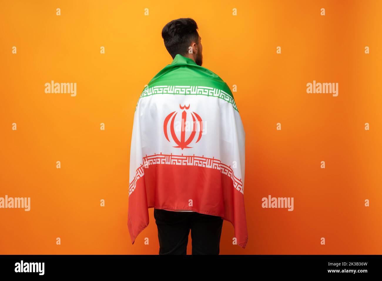 Portrait of a young casual man holding flag of Iran against orange ...