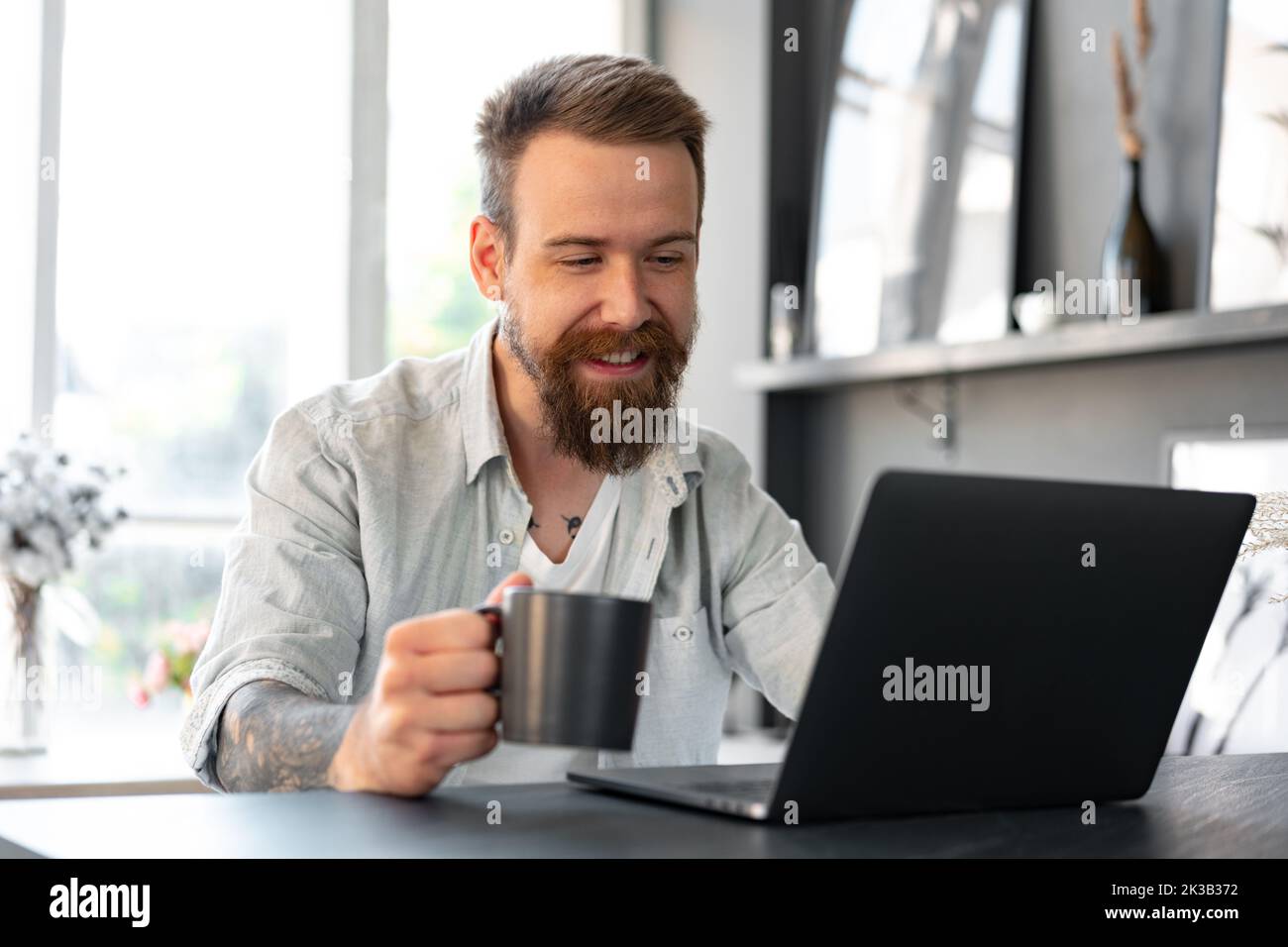 Stylish bearded man working on laptop from home sitting at the table ...