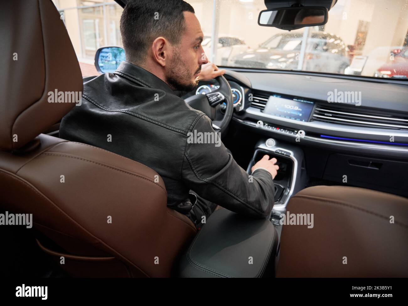 Back view of handsome young man testing new car at dealership, sitting ...