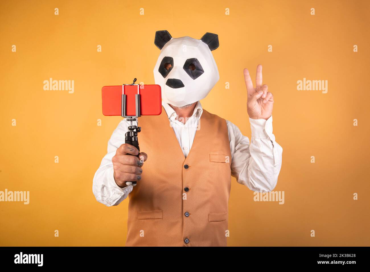 Man in panda bear mask using smartphone for self portrait on yellow ...