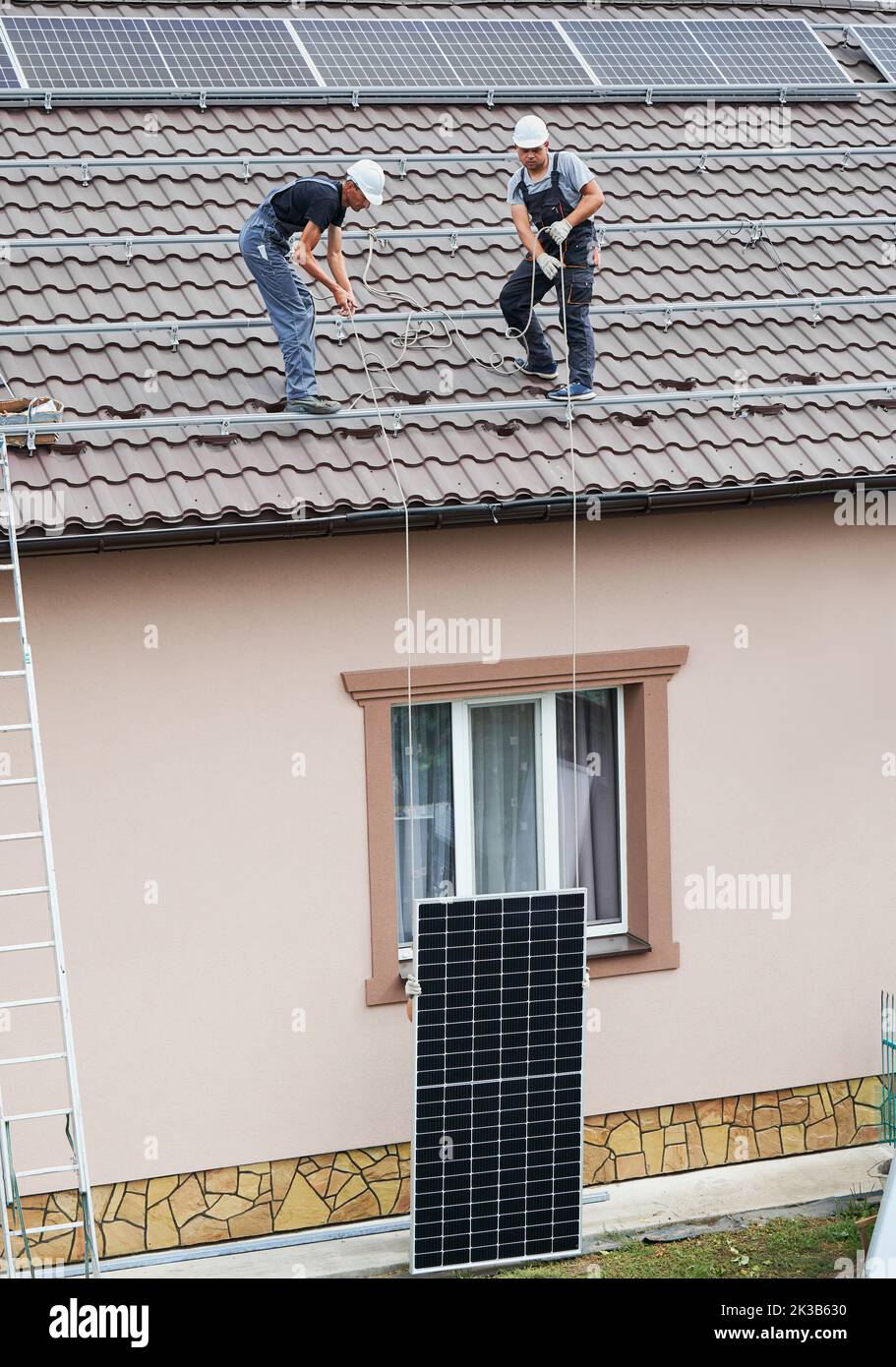 Men technicians lifting up photovoltaic solar moduls on roof of house ...