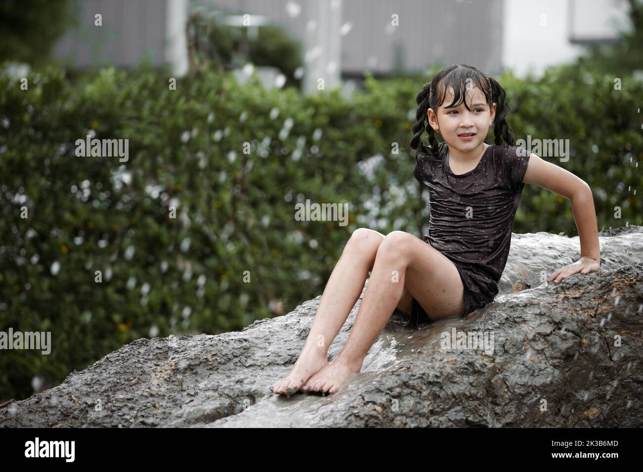 Cheerful child girl playing on heap of wet soil during raining in rainy ...