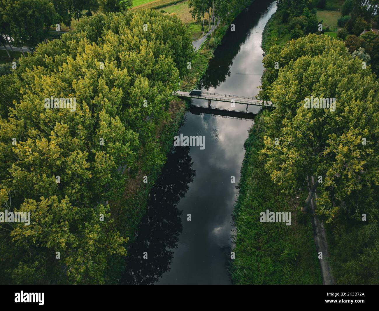 Aerial view of grey van driving over bridge over tree lined canal of ...