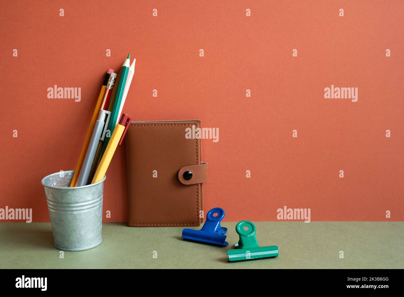 Note, pencil holder, clip on khaki desk. red wall background. workspace ...