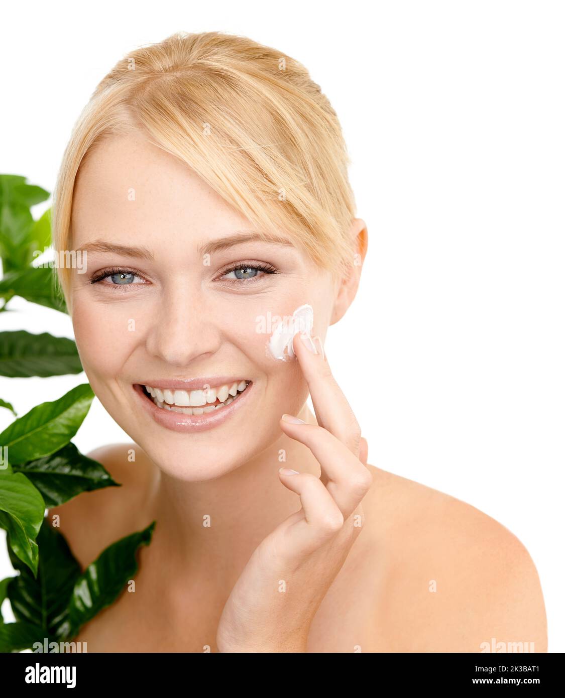 Naturally beautiful. A young woman applying cream to her face while ...