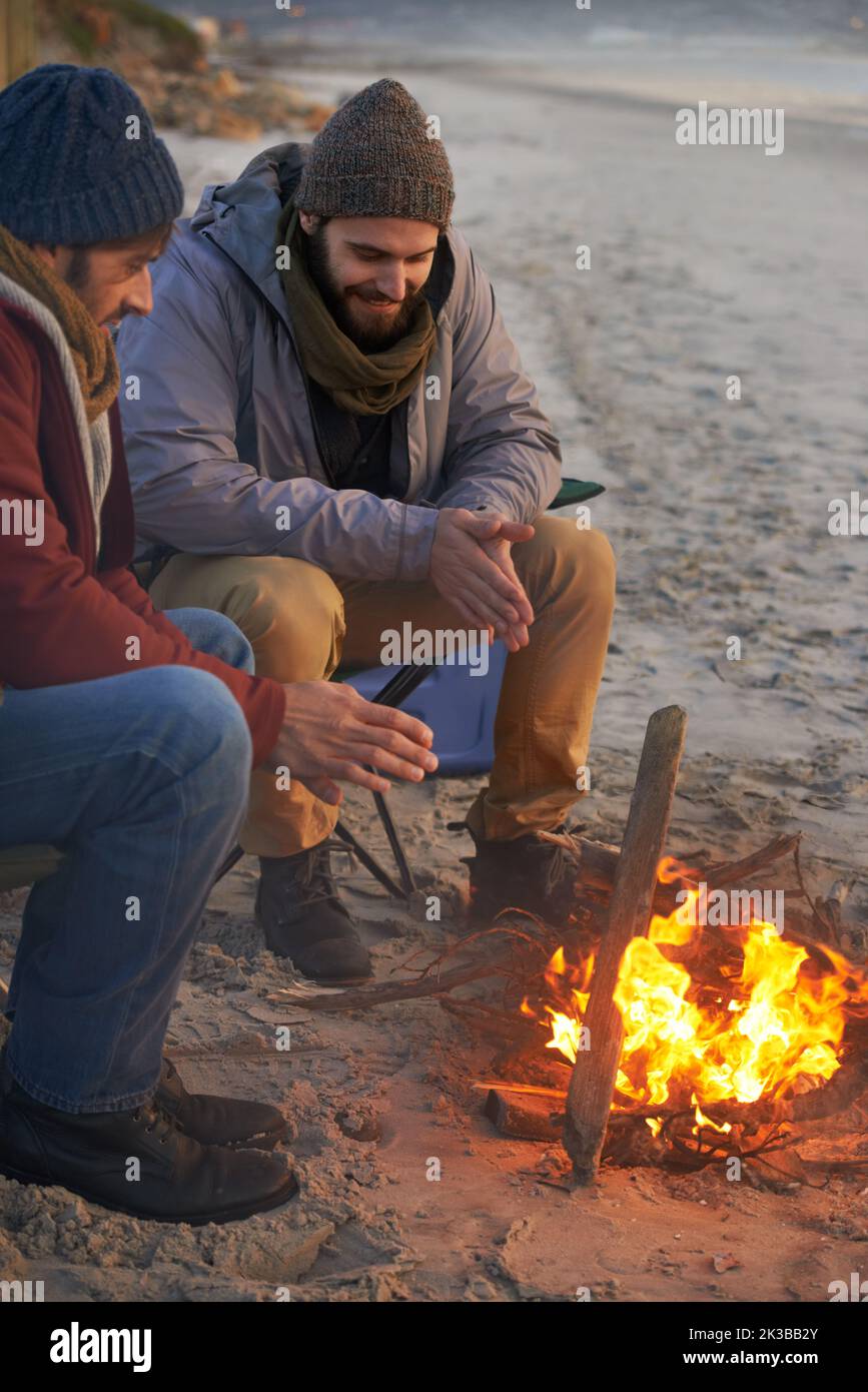 Warming up by the fire. Two young men sitting around a fire on the ...