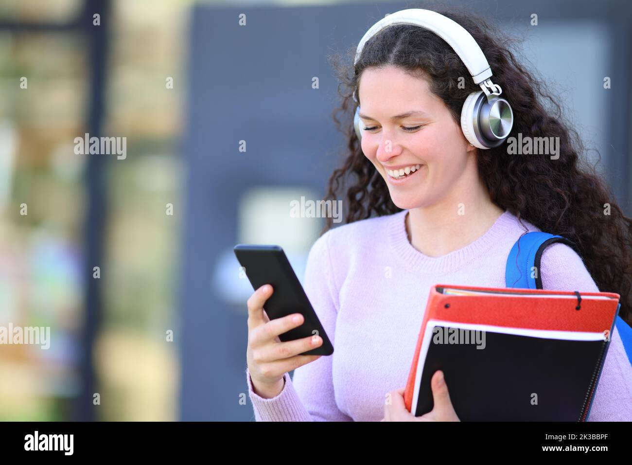 Happy student wearing headphones walks listening audio on phone Stock ...