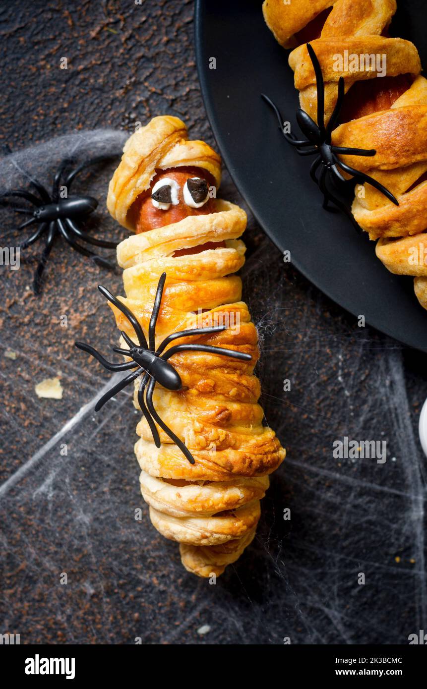 Spooky sausage mummies in dough in black plate with graves on dark ...