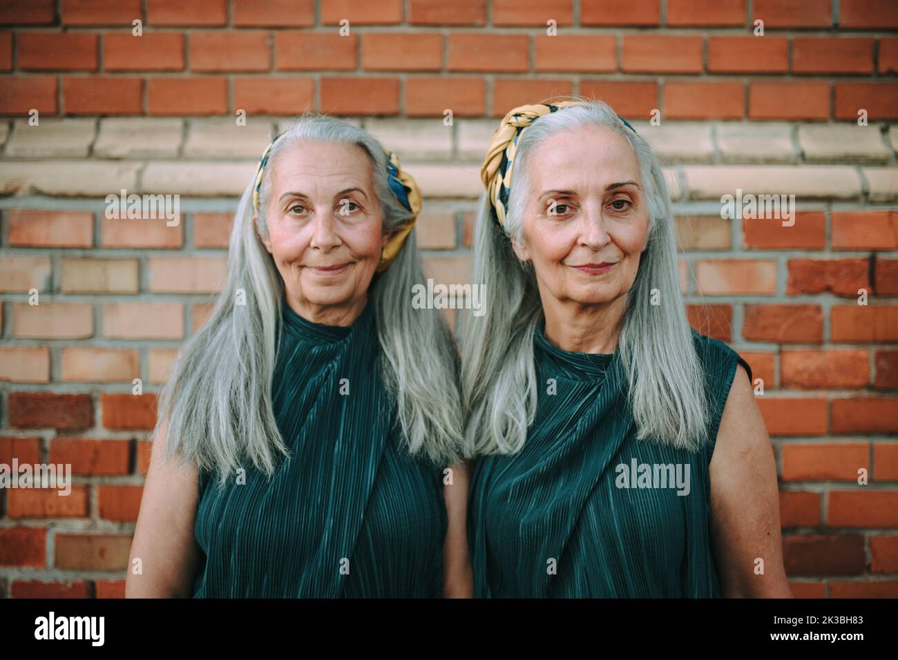 Portrait of senior women, twins,in same clothes standing back to back ...
