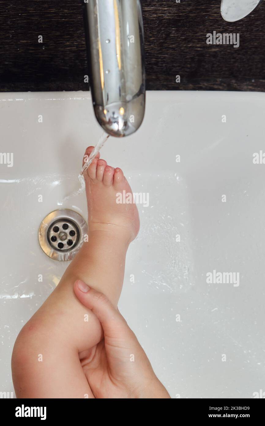 Woman mother washes legs of toddler baby in sink with faucet. Mom helps ...