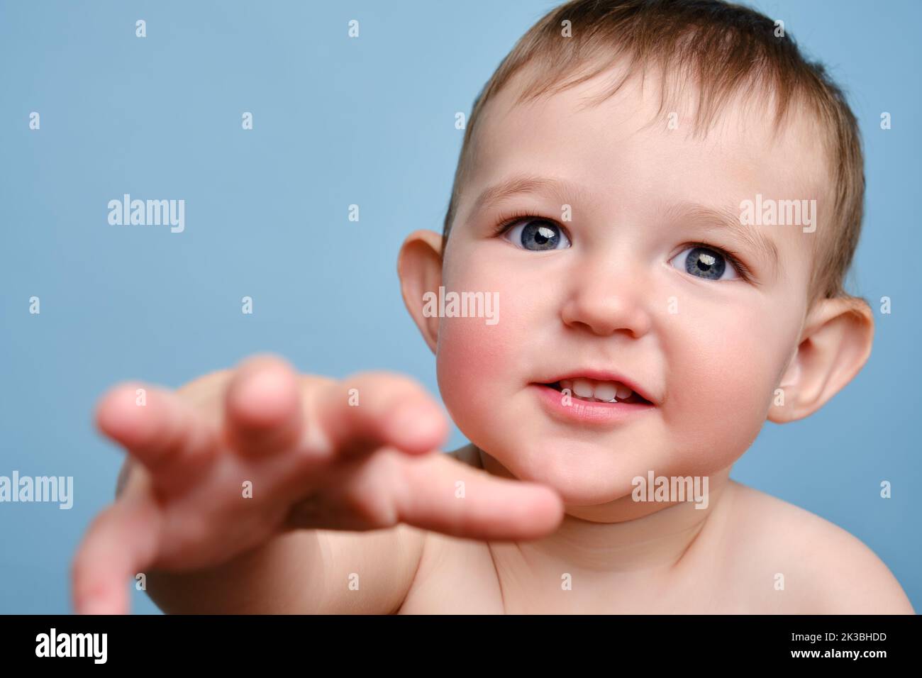 Happy toddler baby boy reaching out with his hand, studio blue ...