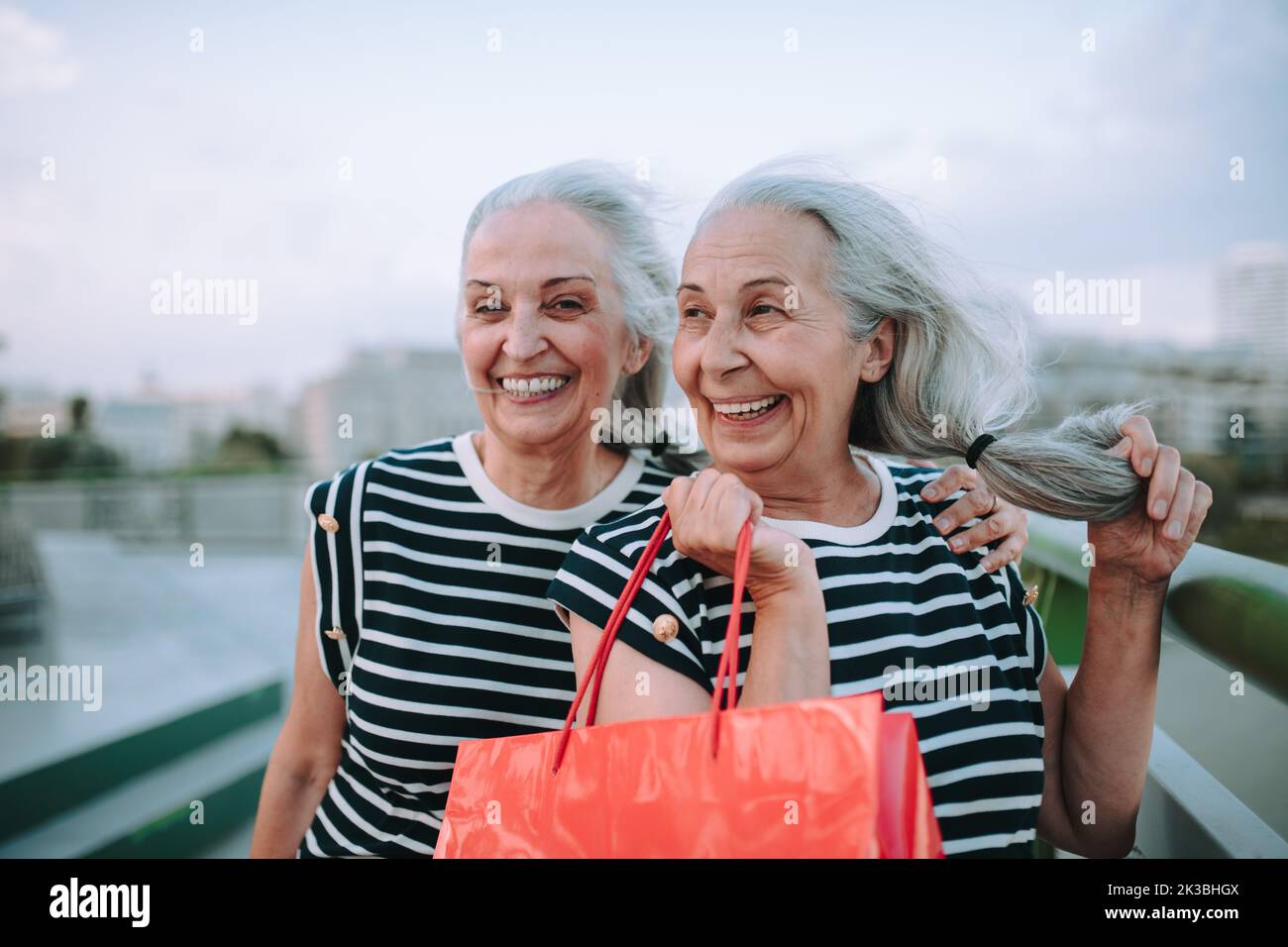 Happy senior twins in same clothes walking in city, returning from ...