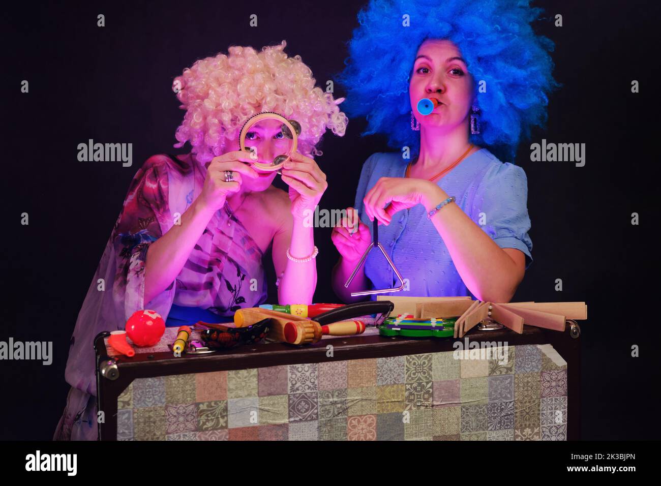 Happy women in funny wigs give a musical performance on a studio black ...