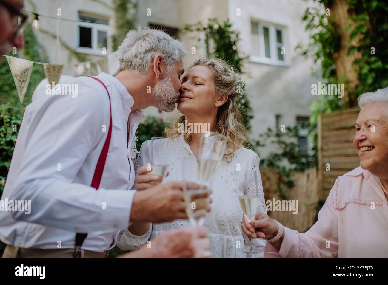 Mature bride and groom kissing at wedding reception with their family ...