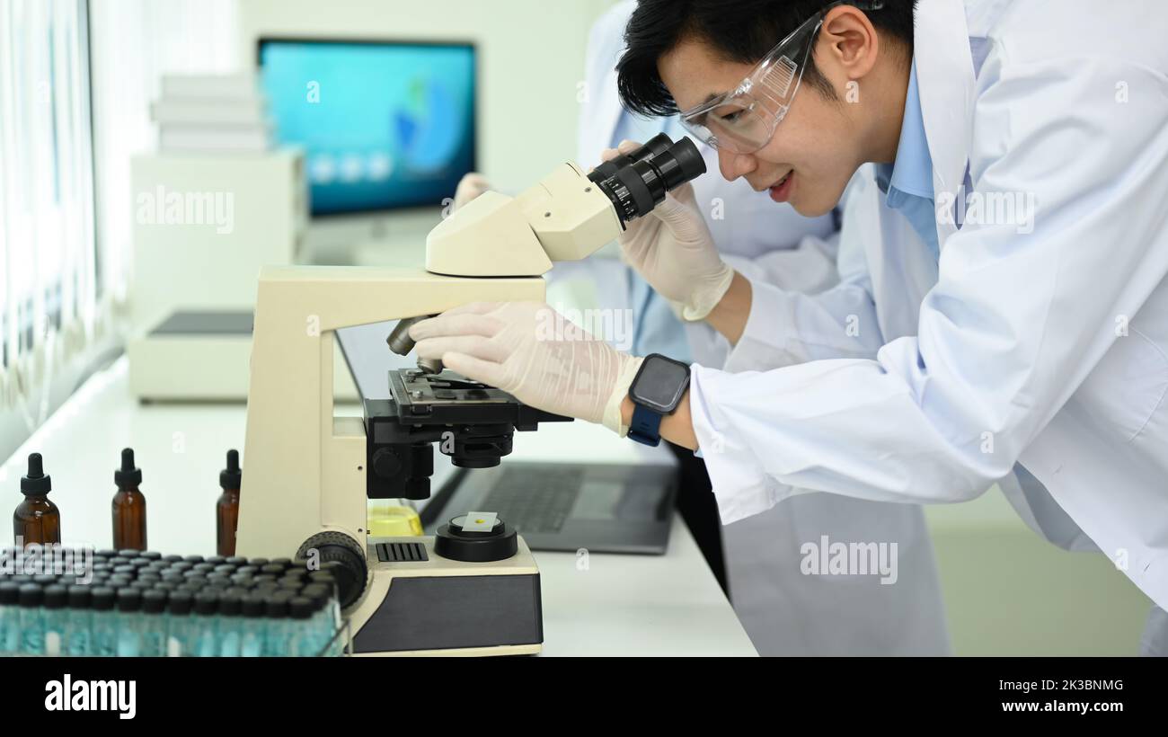 Professional biotechnology specialist looking under microscope ...