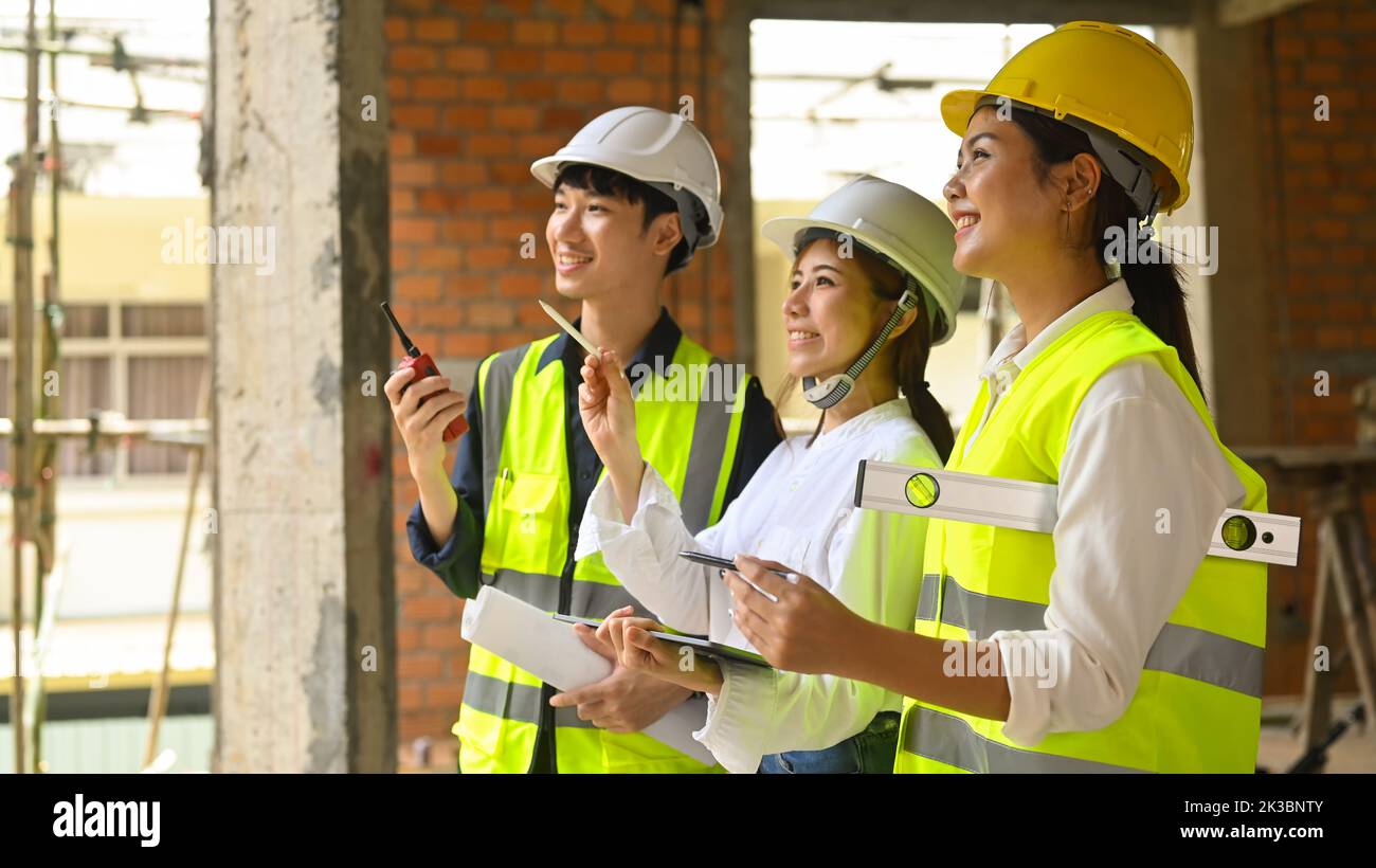 Smiling female investor and engineer managers wearing safety helmet working, checking plan ...