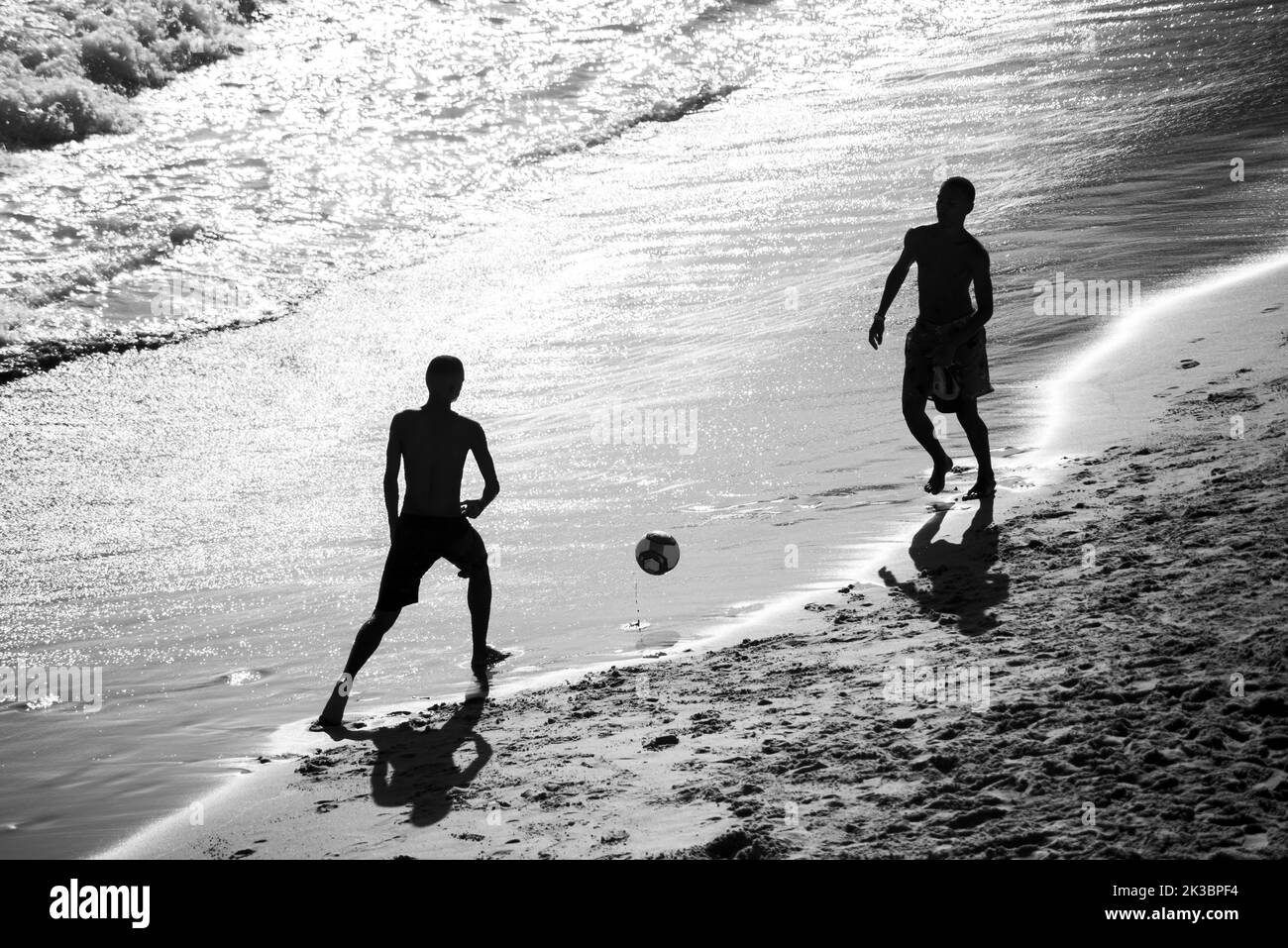A grayscale shot of two young men playing football on the beach ...