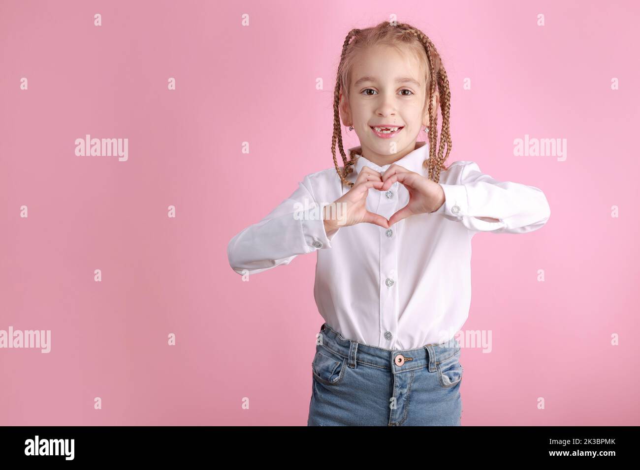 Smiling child girl showing heart sign on pink background. Kid making ...
