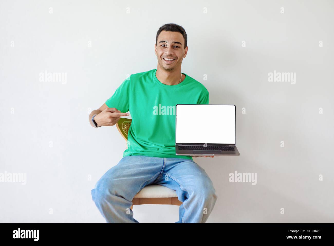 Happy arab man pointing at laptop pc with empty screen, sitting on ...