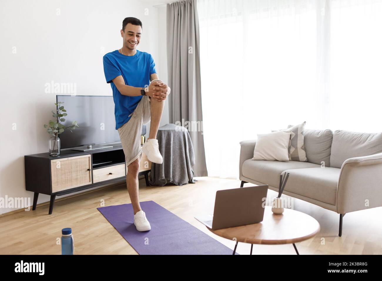 Happy arab man stretching his leg in front of laptop during domestic ...