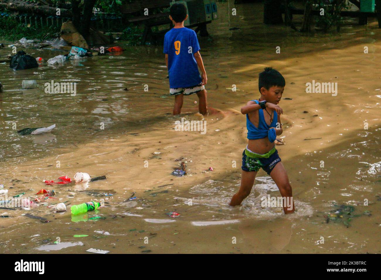 Kids walk on a flooded area with floating plastic wastes after the ...