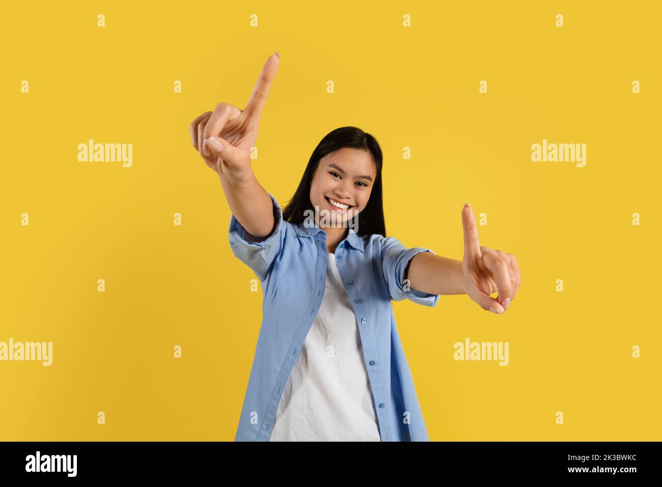 Cheerful young chinese woman student in casual show fingers up to copy ...