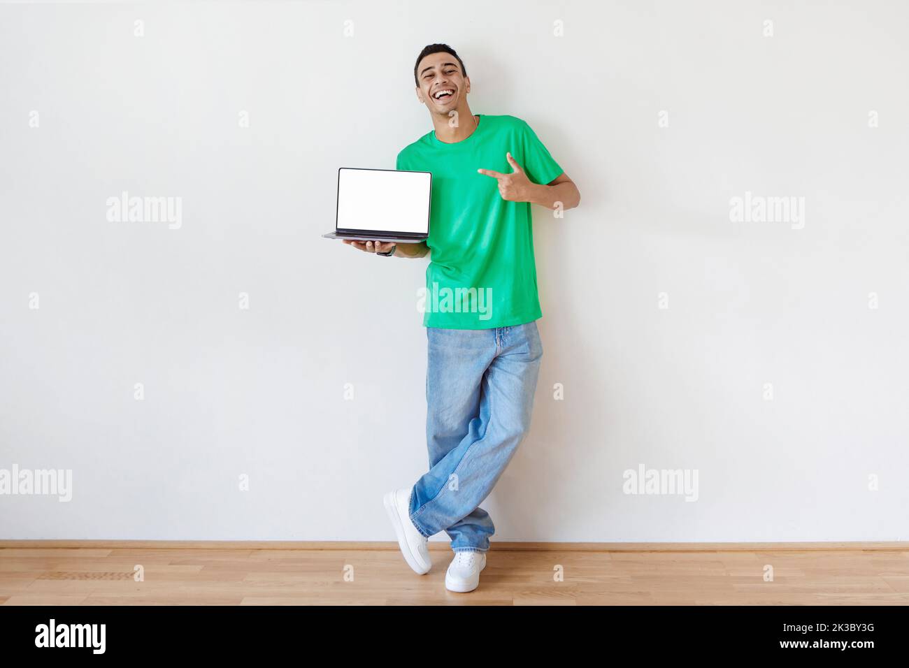 Happy young arab man pointing at laptop with blank screen against light ...