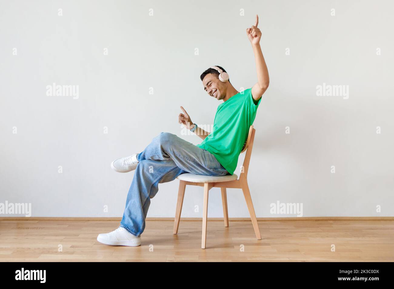 Cheery guy in headphones listening to music and dancing while sitting ...