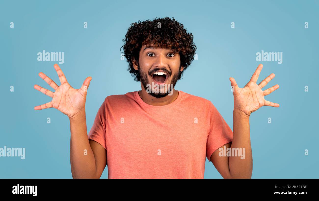 Amazed hindu guy raising hands up over blue background Stock Photo - Alamy