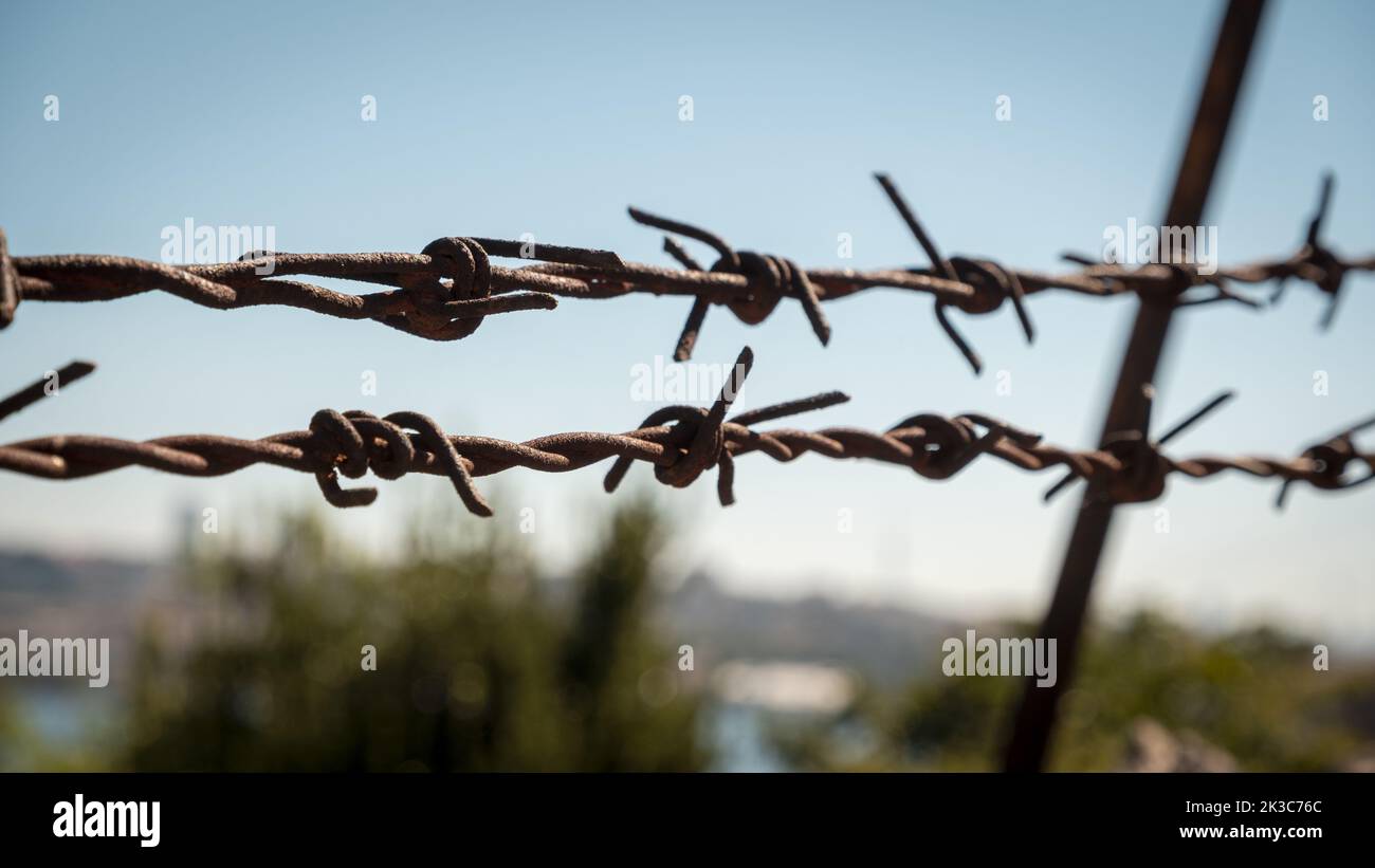 Close up to barbed wire with blue sky and landscape in the background ...