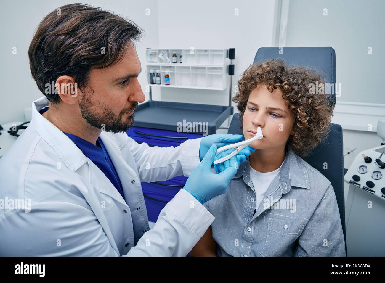 ENT using nasal speculum or rhinoscope to examine child patient's nose ...