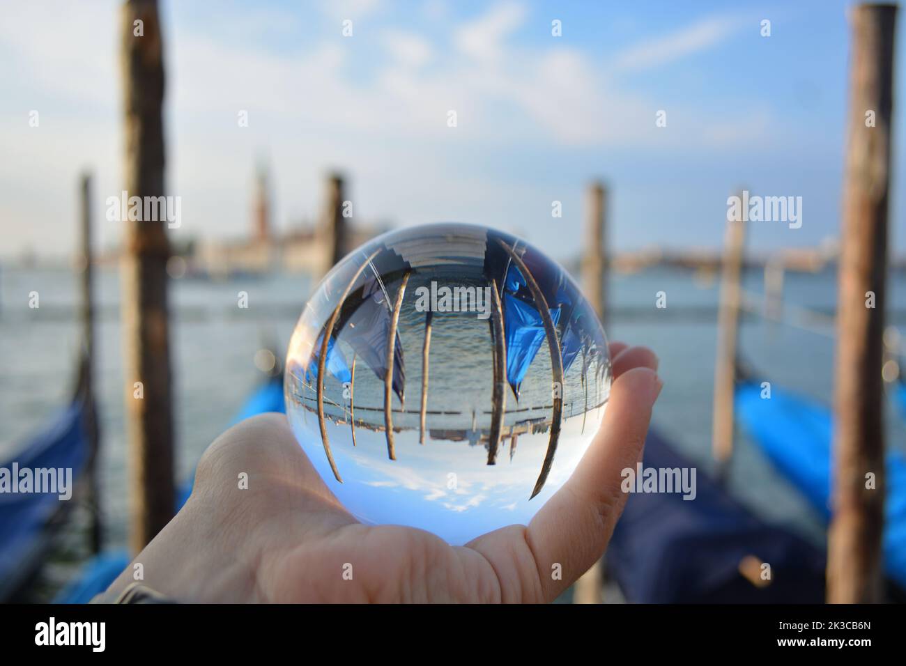 Hand holding glass sphere in front of lagoon and gondola, sunny day in ...