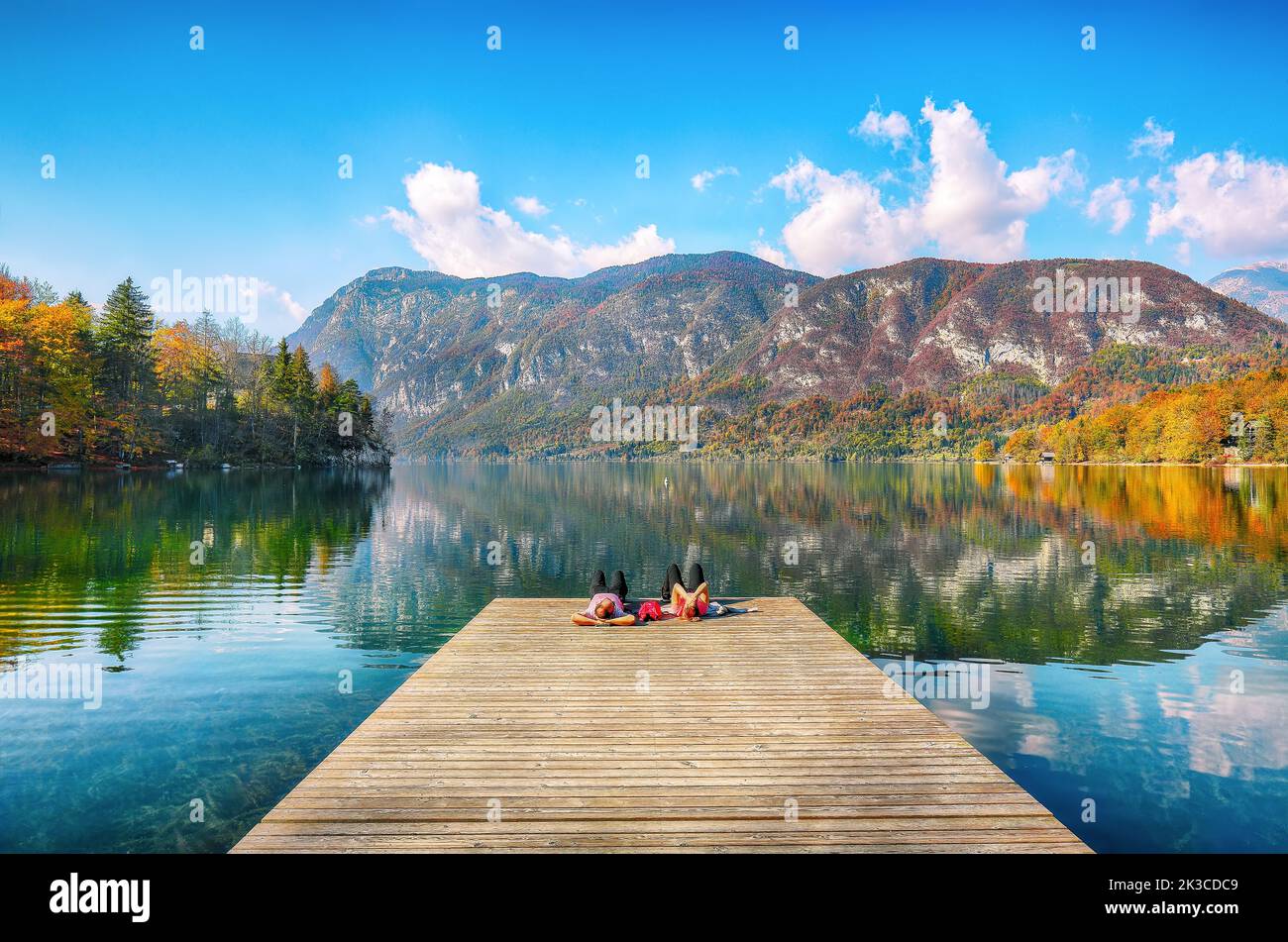 Fabulous view of Bohinj Lake with couple lying on a wooden pier ...