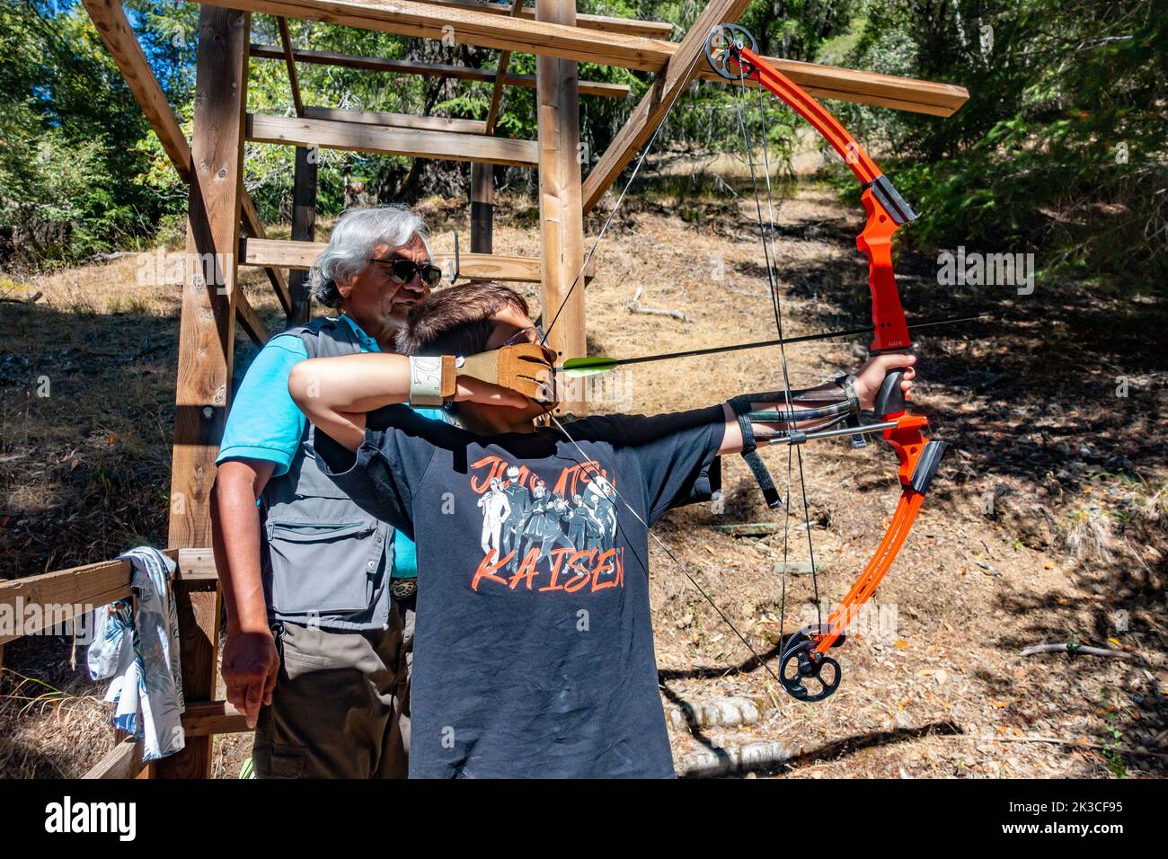 A boy has a go at archery, bow drawn ready to shoot. Supervised by an ...