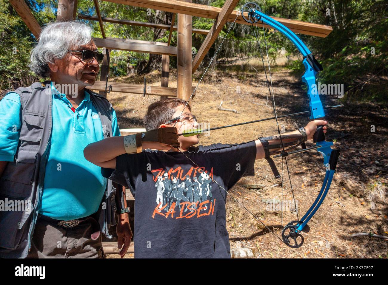 A boy has a go at archery, bow drawn ready to shoot. Supervised by an ...