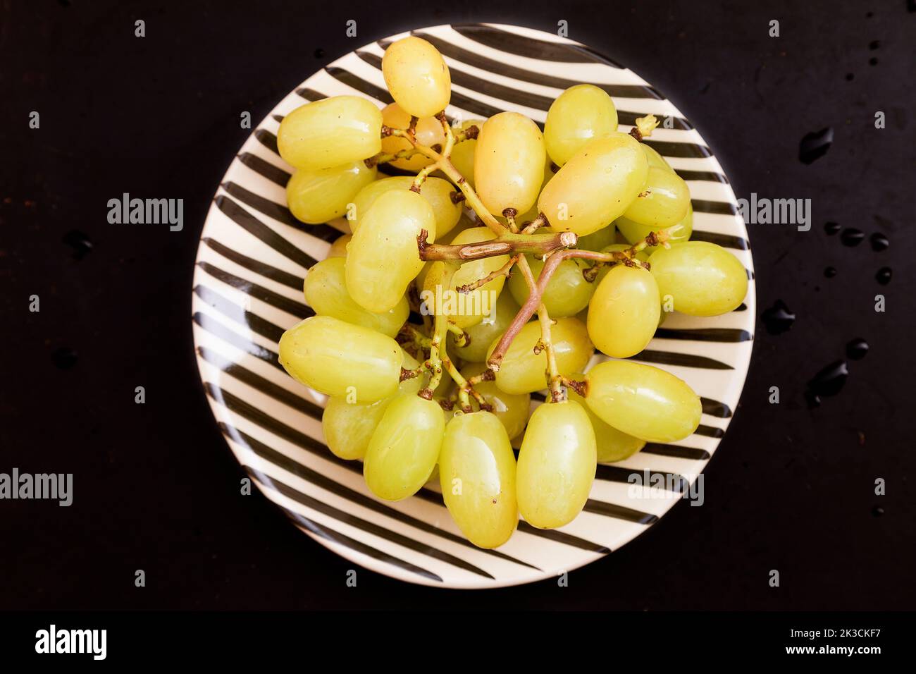 a cluster of ripe grapes in a striped plate over a black background ...