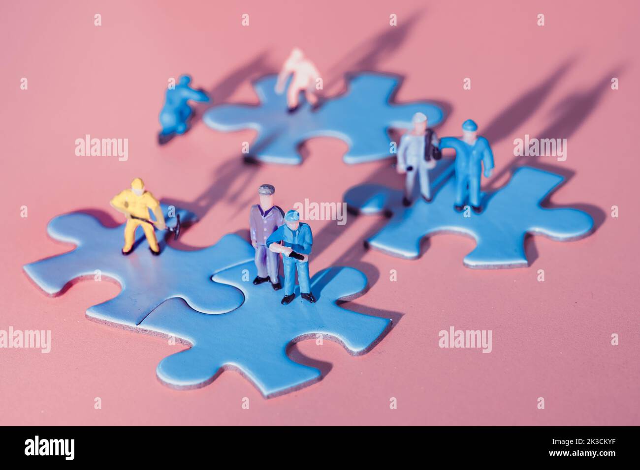 Team of tiny worker miniature figures on linked jigsaw puzzle pieces ...
